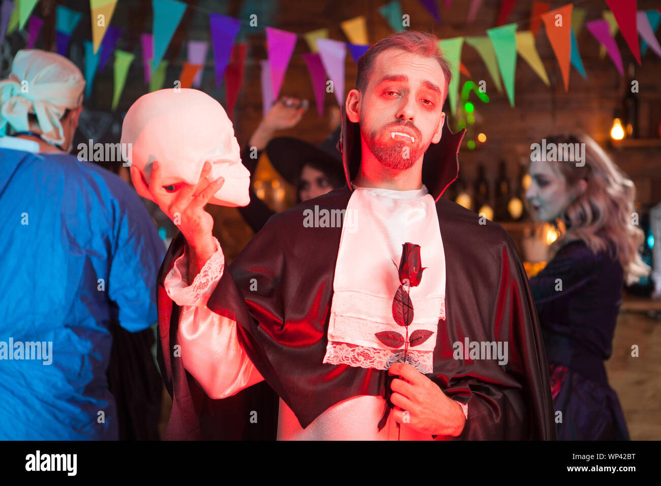 Attractive man dressed up like vampire with a human skull at halloween ...