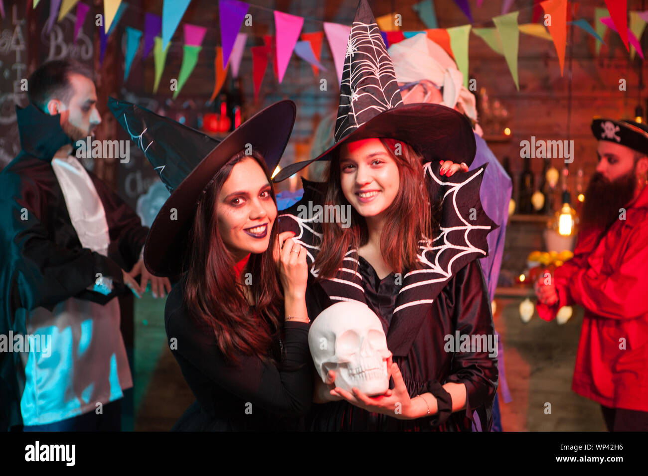 Beautiful young witch holding a human skull and smiling to the camera ...