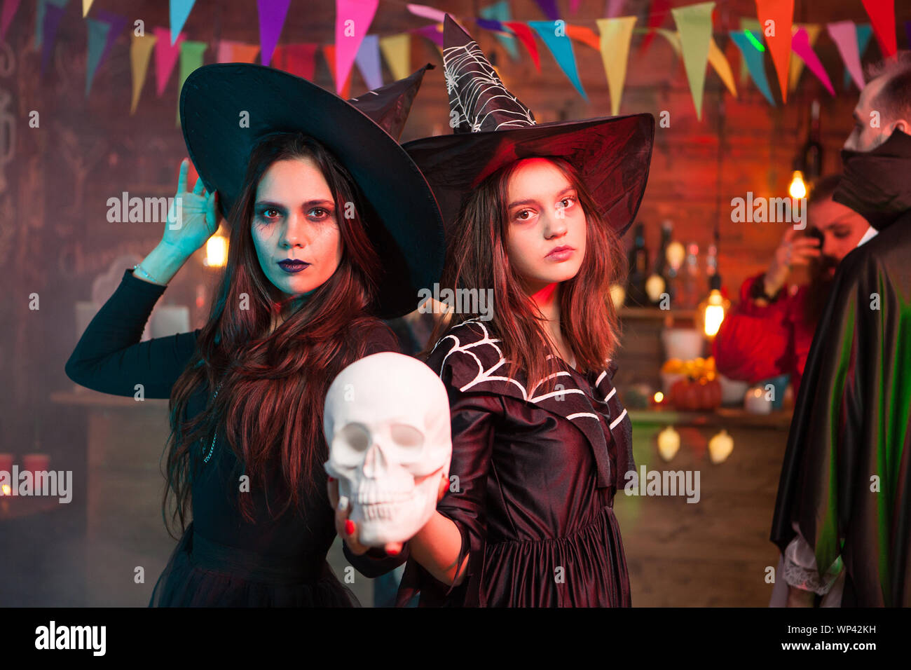 Two beautiful girls in black dresses and witch's hats hold a skull for ...