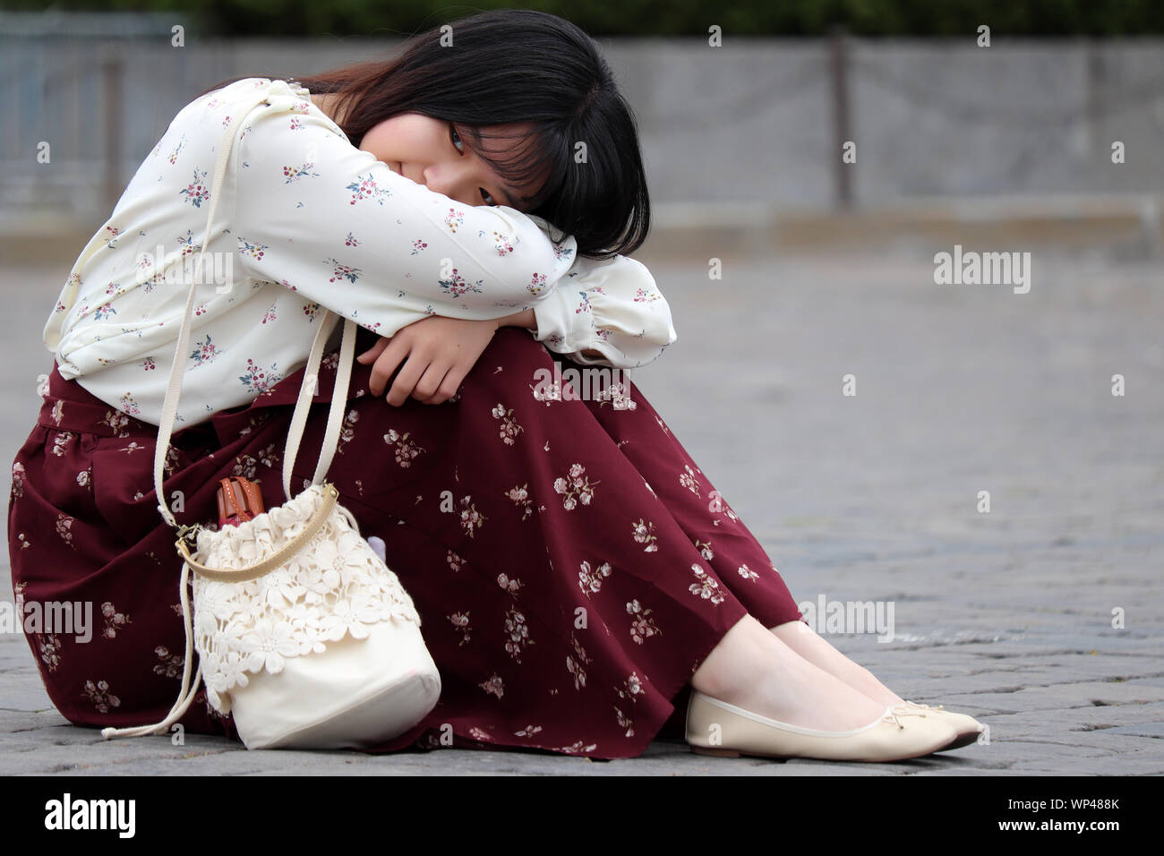 Pretty asian girl sitting on the street with her arms around her knees ...