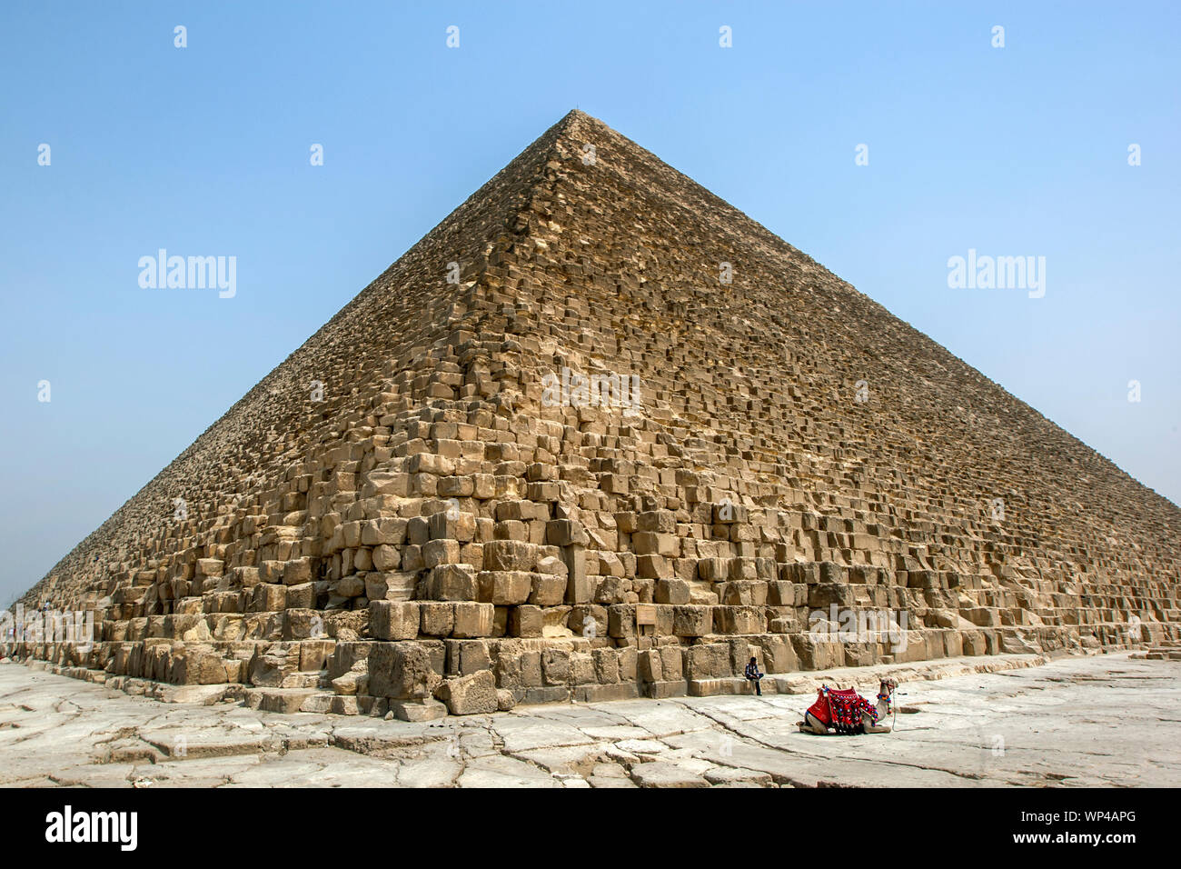 A man and a camel sit beside the giant stone blocks of the Pyramid of ...