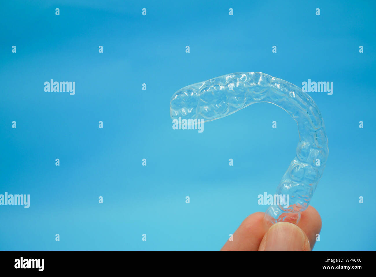 hand holding clear plastic retainer teeth that isolated on blue sky ...