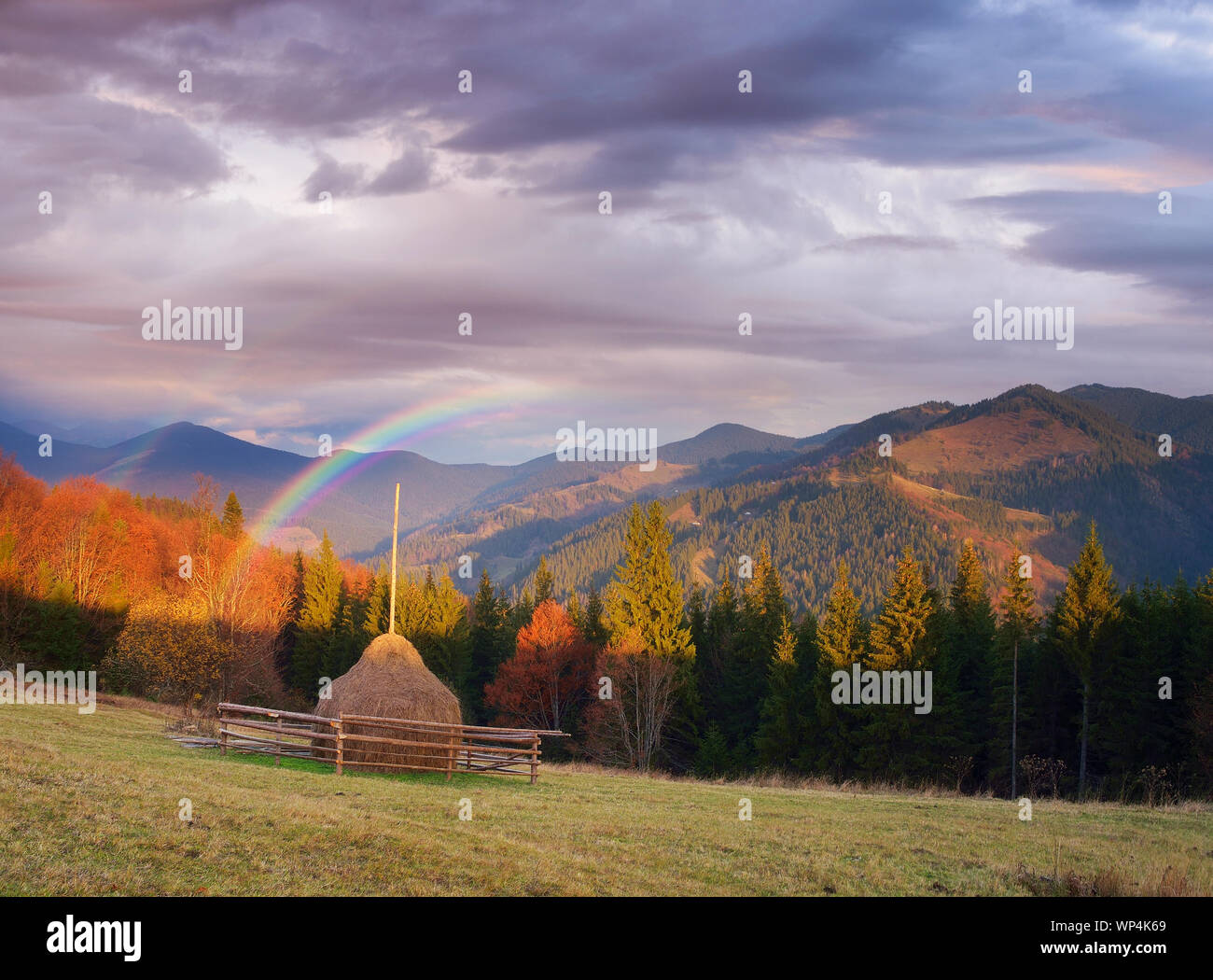 Autumn landscape in a mountain village. Haystack on the meadow. Rainbow ...