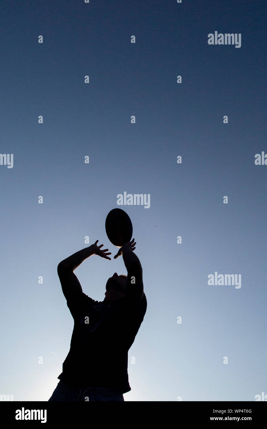 A boy catching and passing a rugby ball on a summer's day in a park ...