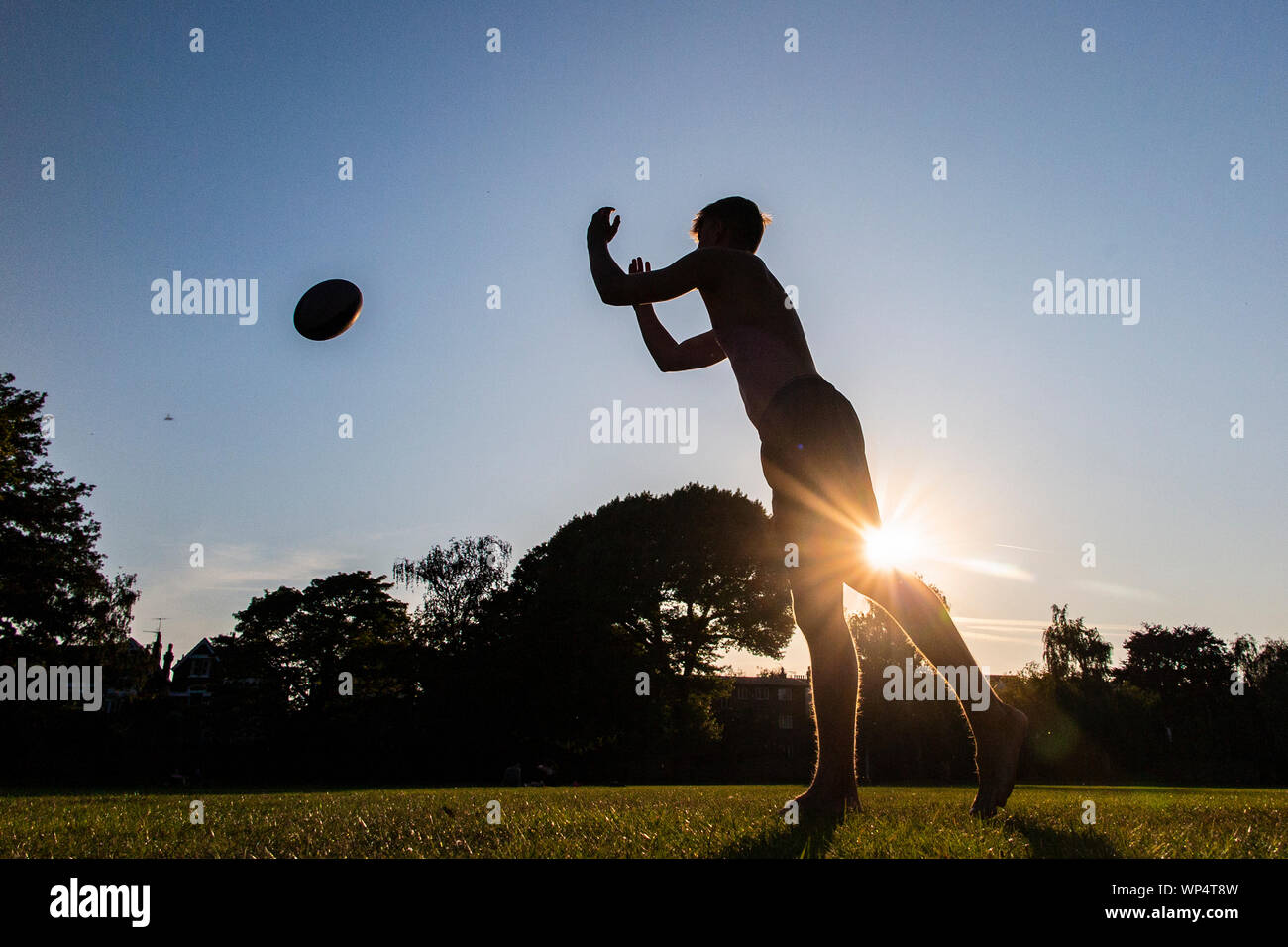 A boy catching and passing a rugby ball on a summer's day in a park ...