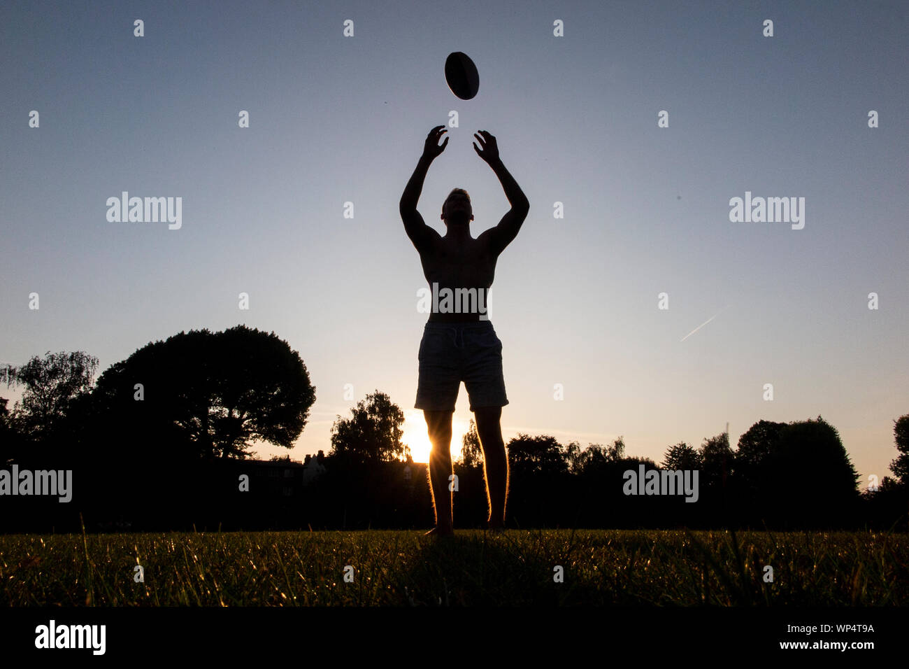 A boy catching and passing a rugby ball on a summer's day in a park ...
