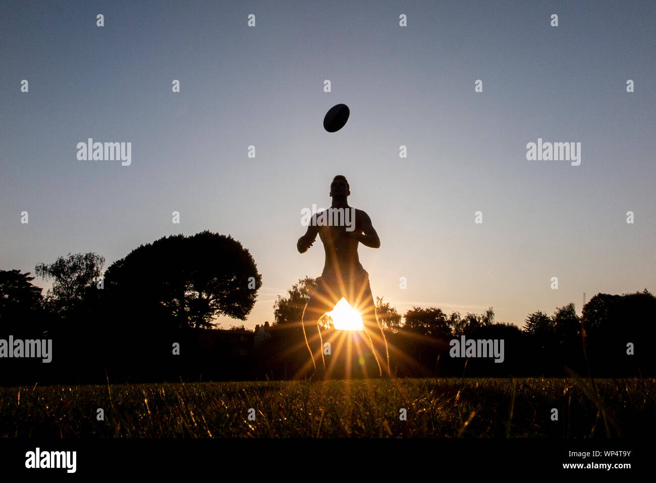 A boy catching and passing a rugby ball on a summer's day in a park ...