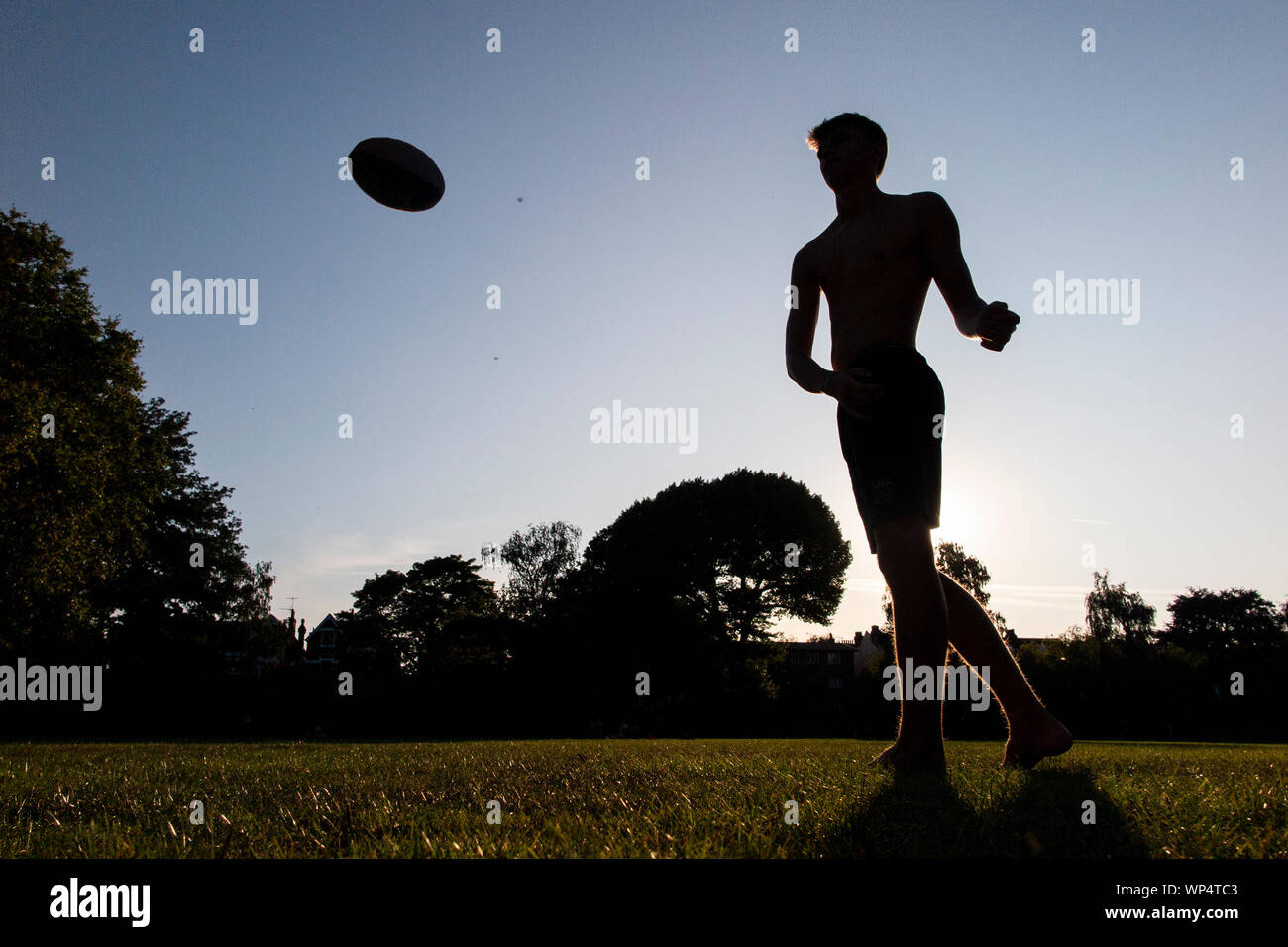 A boy catching and passing a rugby ball on a summer's day in a park ...