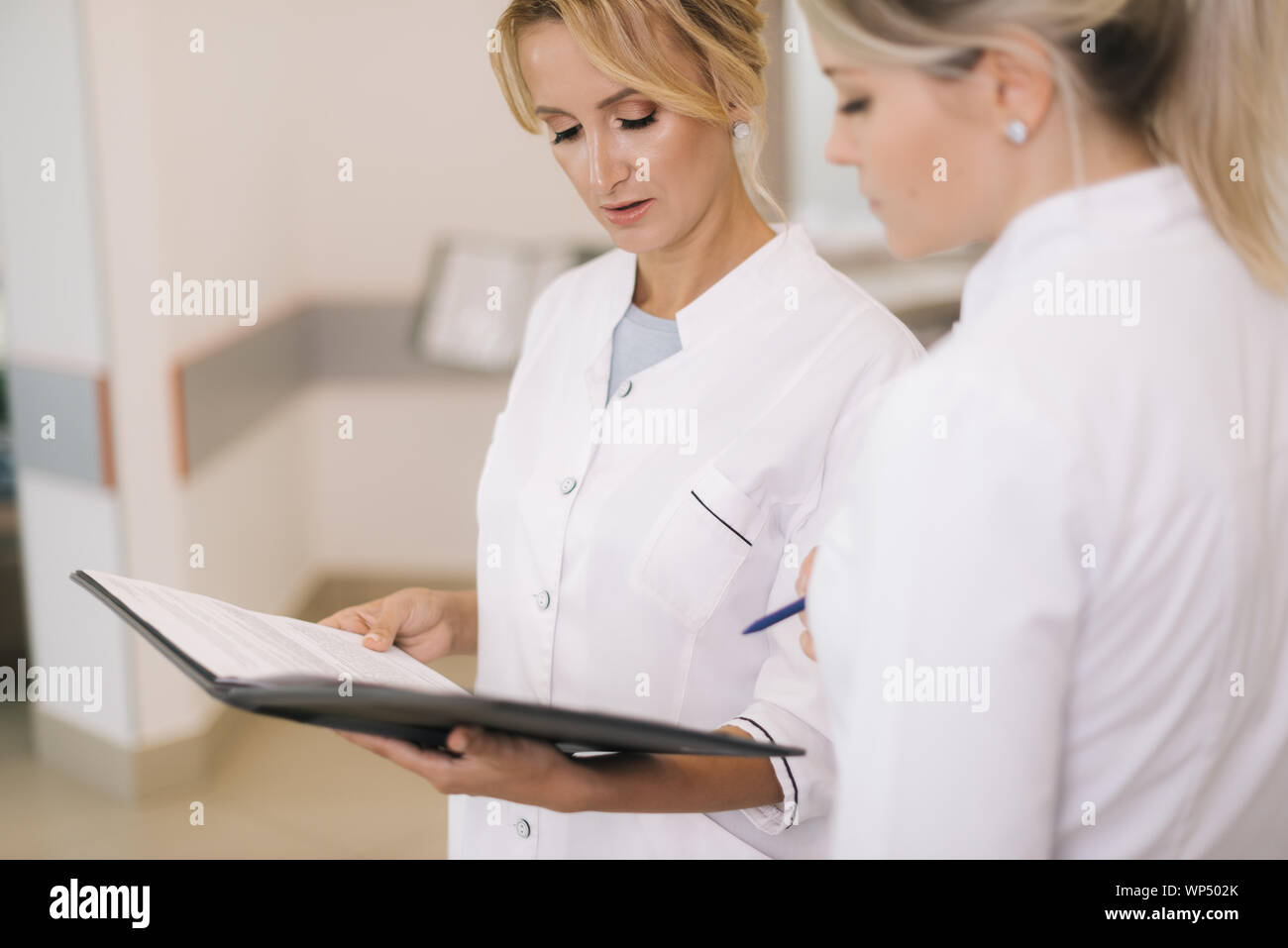 Two women doctors standing with clipboard at hospital and discussing ...