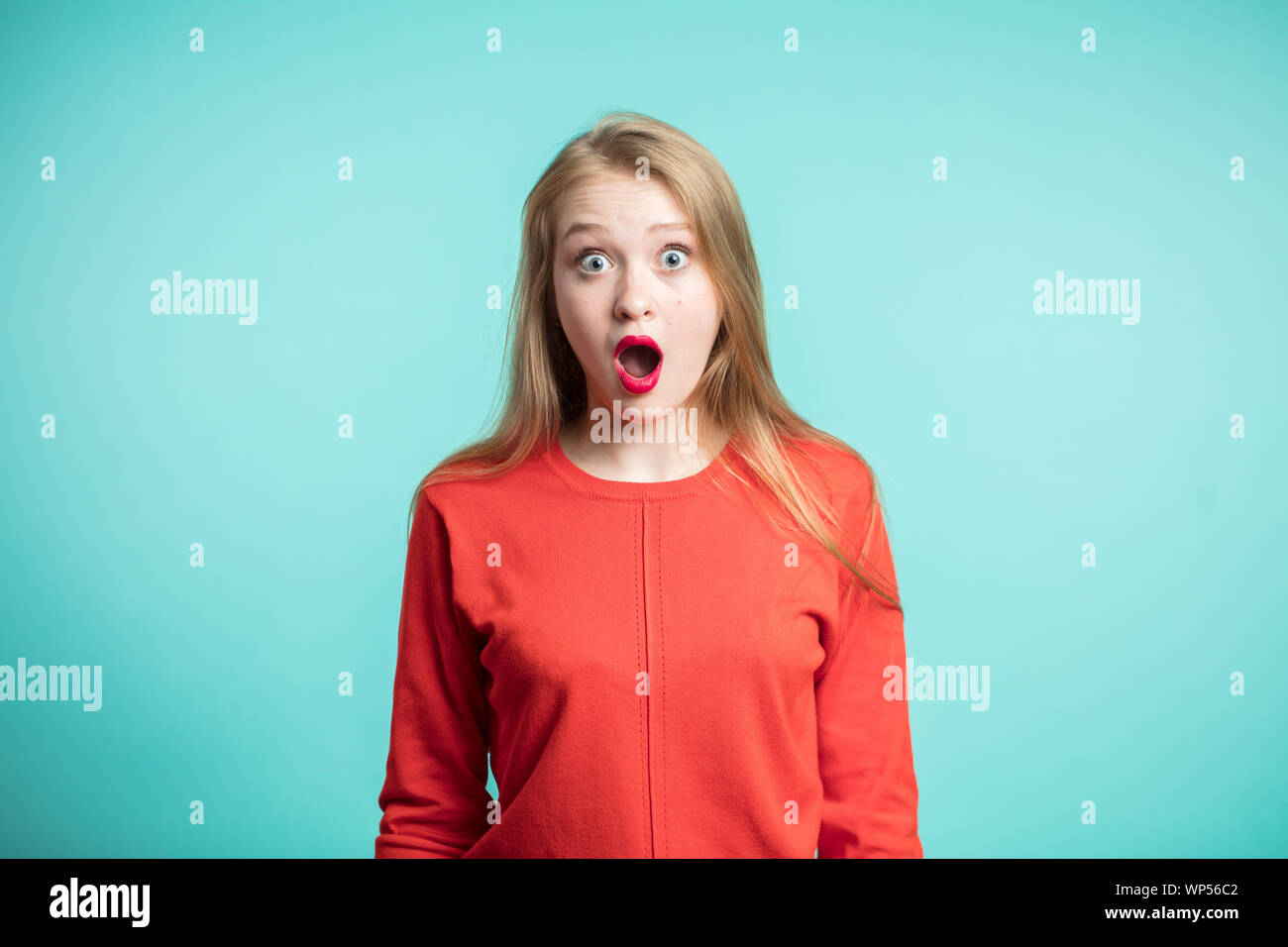 Surprised young woman shouting on blue background. Looking at camera ...