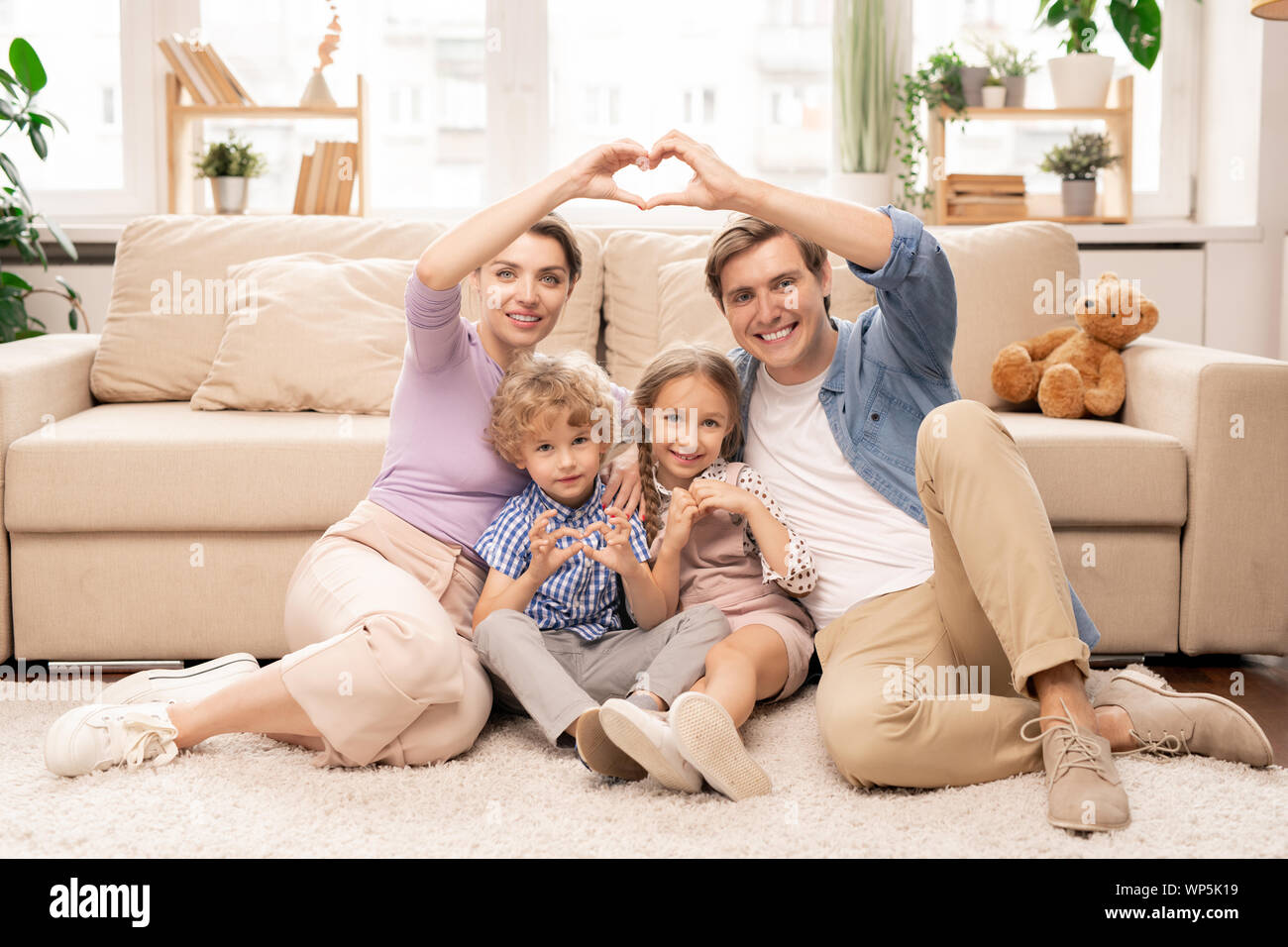 Happy parents and two adorable siblings making heart shape with fingers ...
