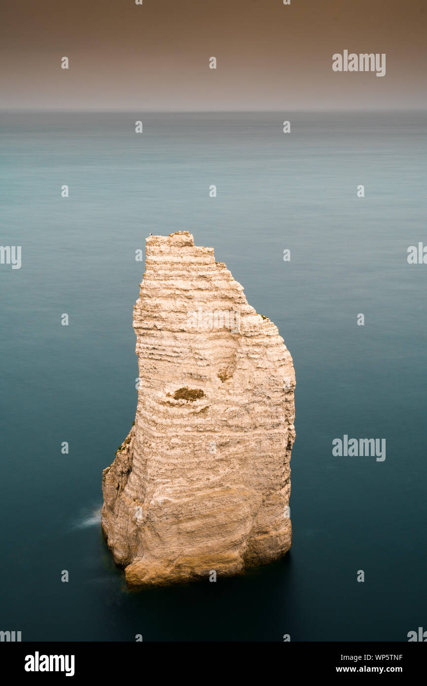 A vertical view of a rock needle granite cliff in a calm dark blue ...