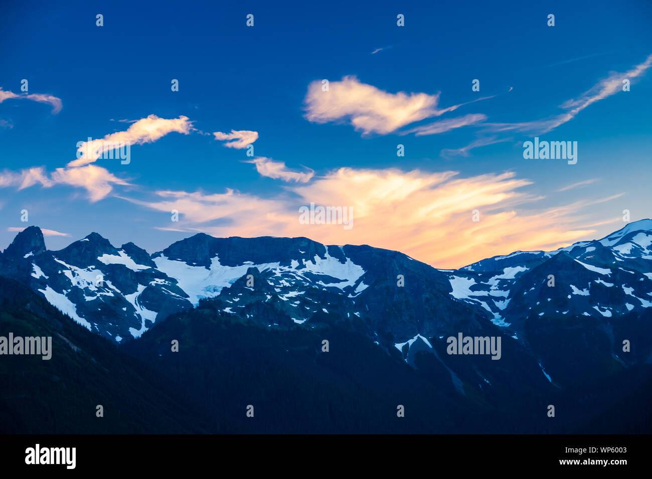 Alpenglow on clouds over a rugged mountain range, Mt. Rainier National ...