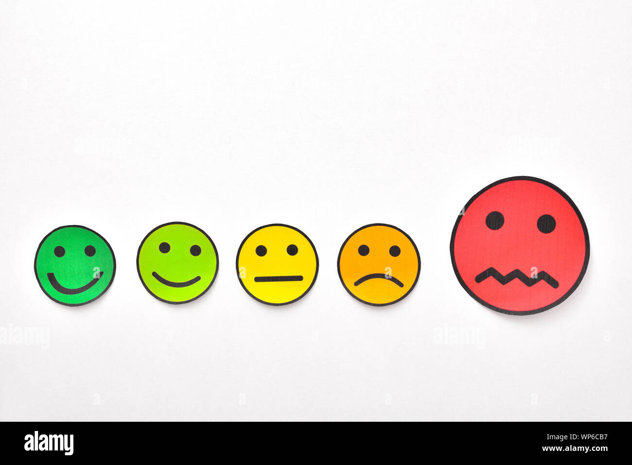 Paper face cutouts on white table highlighting negative rating ...