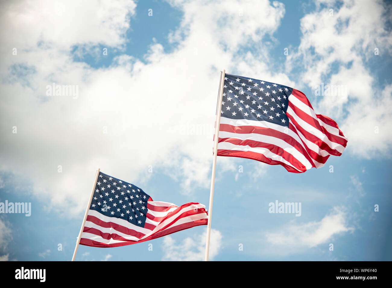 Two American flags fluttering in the wind against a bright blue sky ...