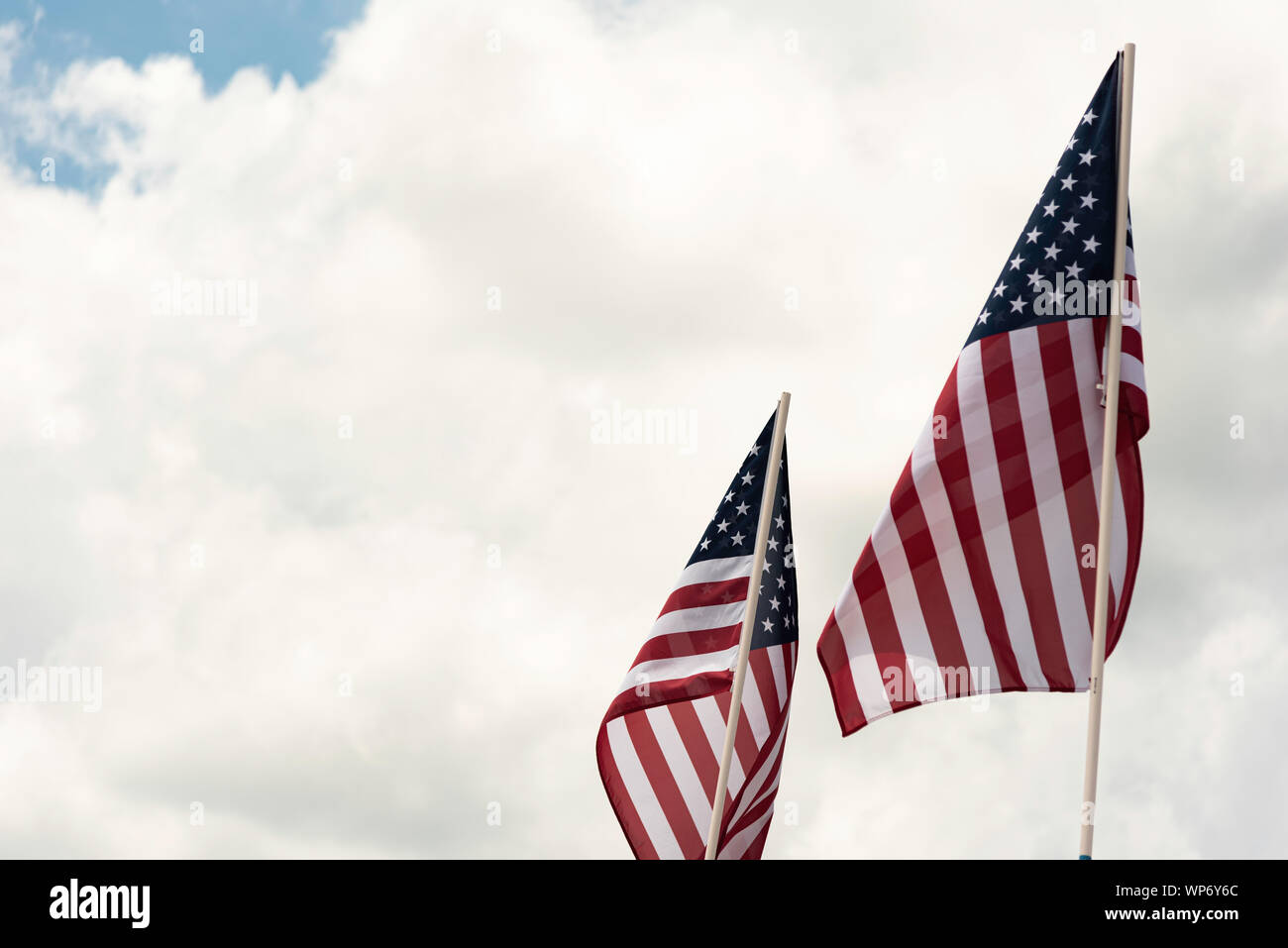Two American flags fluttering in the wind against a bright blue sky ...