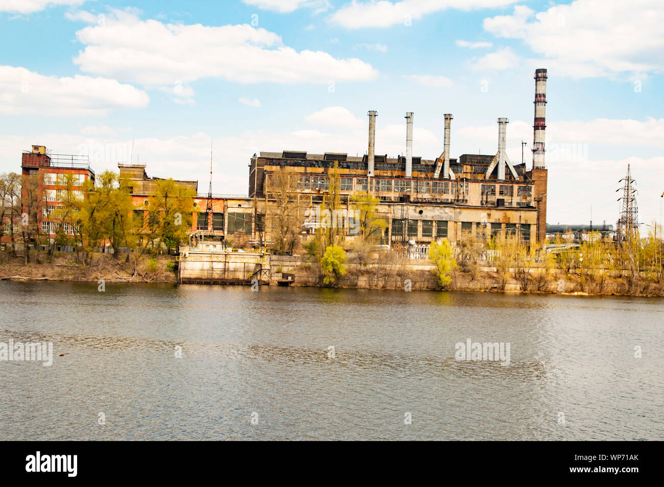 Old industrial factory with pipes on the river bank on a sunny day ...