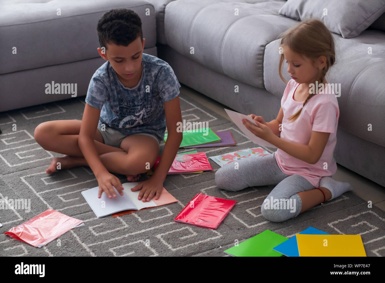 Focused boy and girl in casual clothes putting covers on new copybooks ...