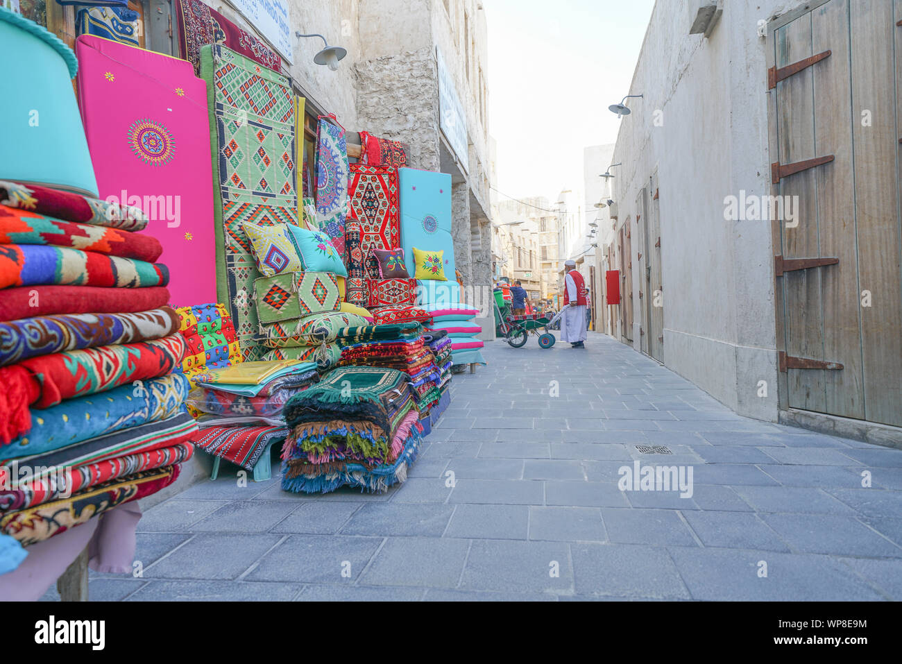 DOHA QATAR - JULY 11 2019; Brightly colored rugs with man in lane and ...