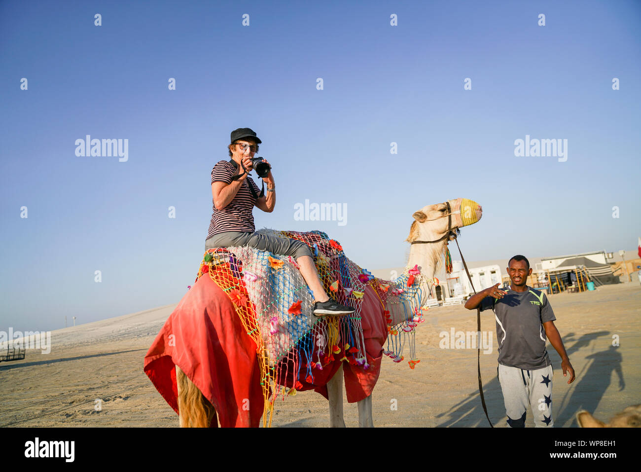 DOHA QATAR - JULY 12 2019; Camel riding photgraphing tourist with camel ...