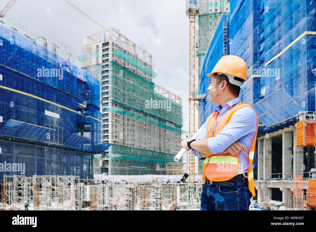 Smiling Asian construction worker with blueprint in his hand turning ...