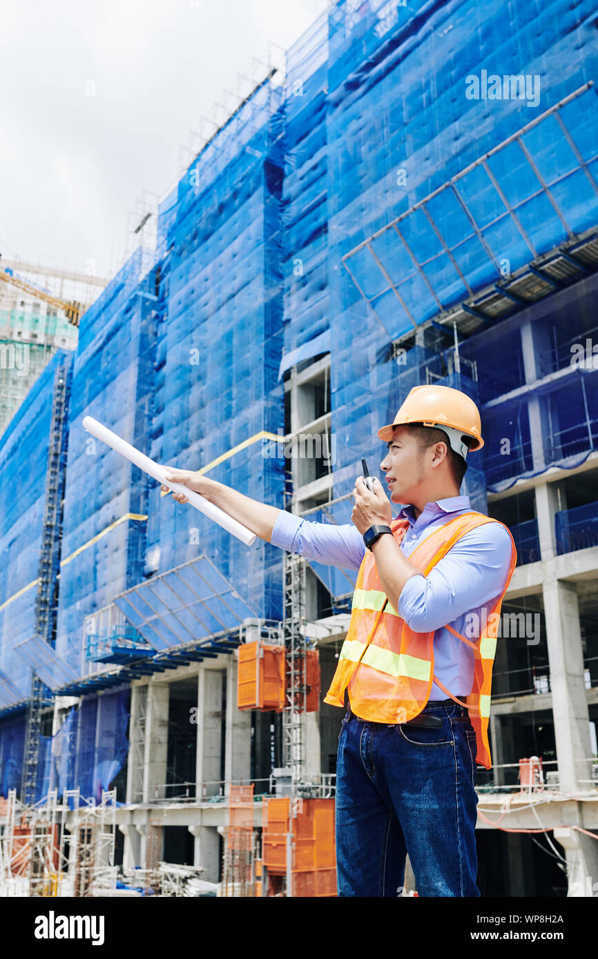Contractor pointing with scroll in his hand and talking on walkie ...
