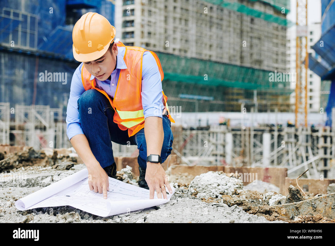 Serious Vietnamese contractor in orange hardhat examining building ...