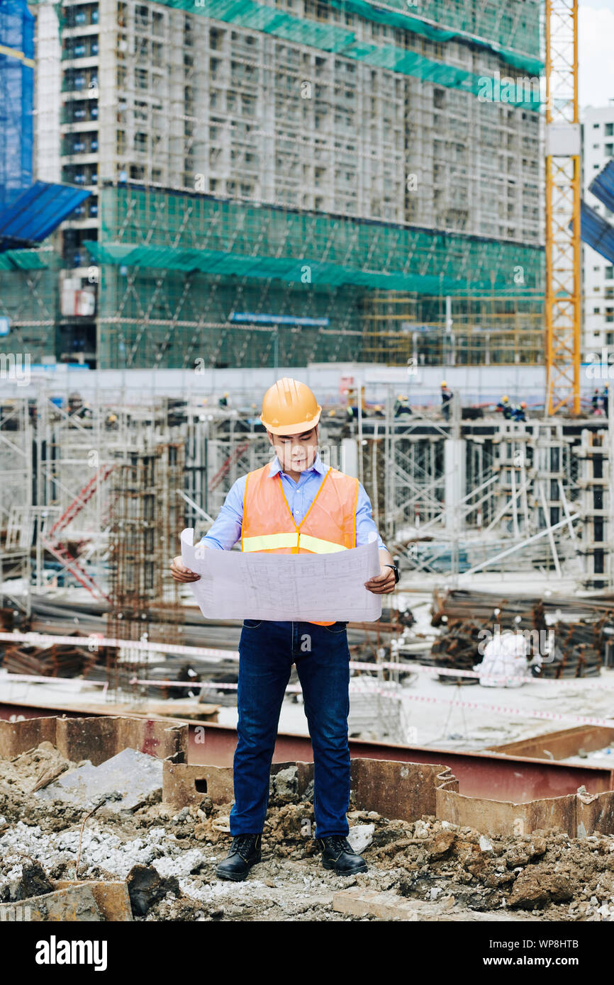Young Vietnamese construction engineer standing at construction site of ...