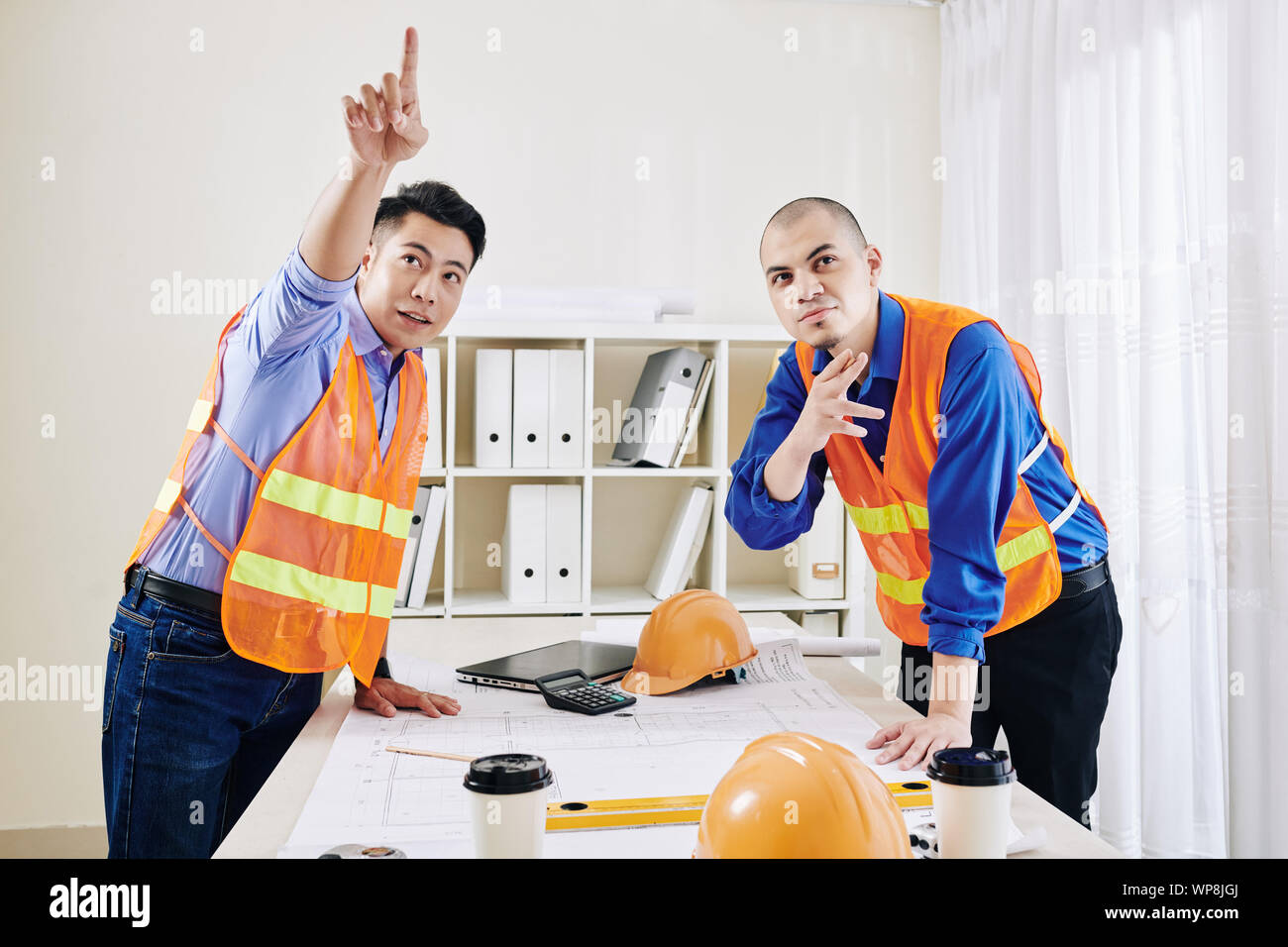 Multi-ethnic team of construction engineers leaning over table with ...