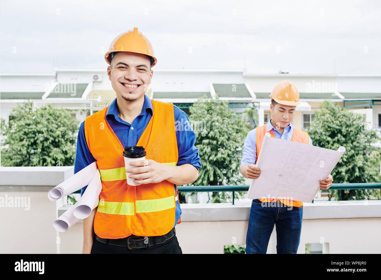 Smiling civil engineer standing outdoors with many blueprints scrolls ...