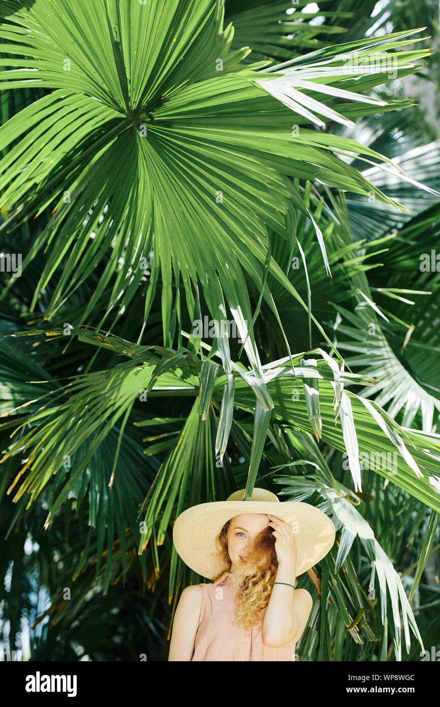 Beautiful young happy woman in straw hat standing under palm tree on ...