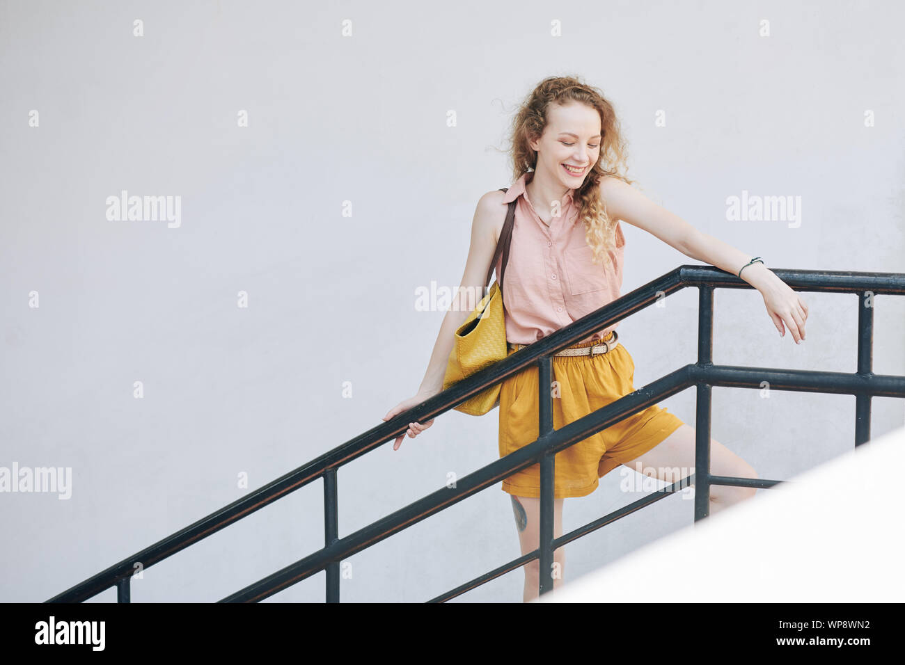 Happy laughing pretty girl leaning on railing and looking down from the ...