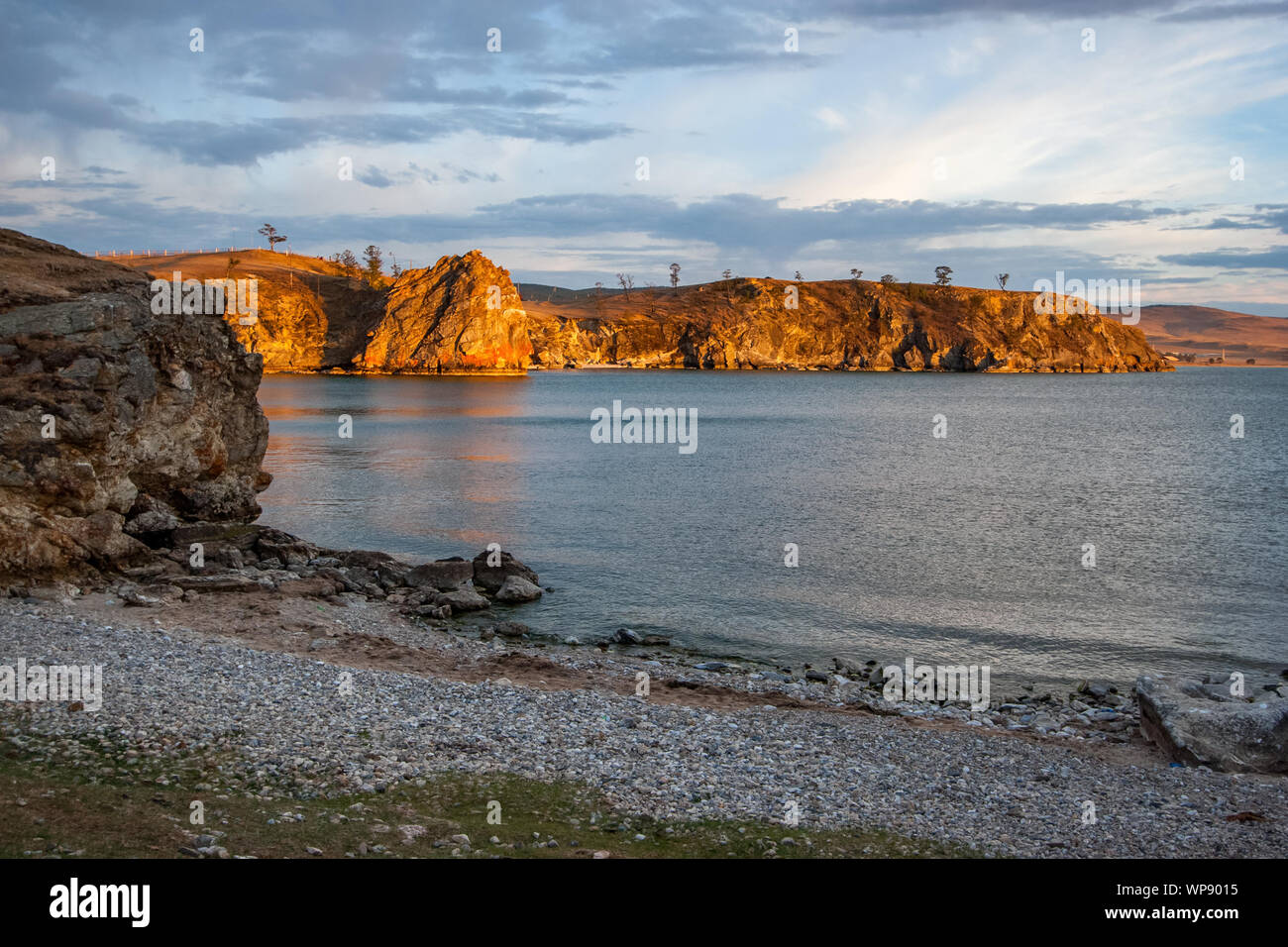 Red rocks on a lake lit by the sun at sunset. Pebble beach. Clouds in ...