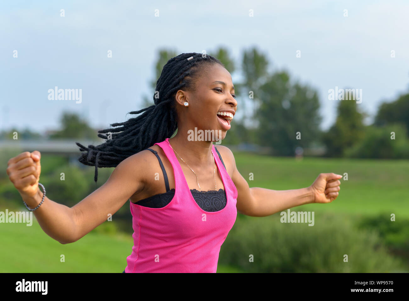 Vivacious young African woman cheering as she runs along a rural path ...