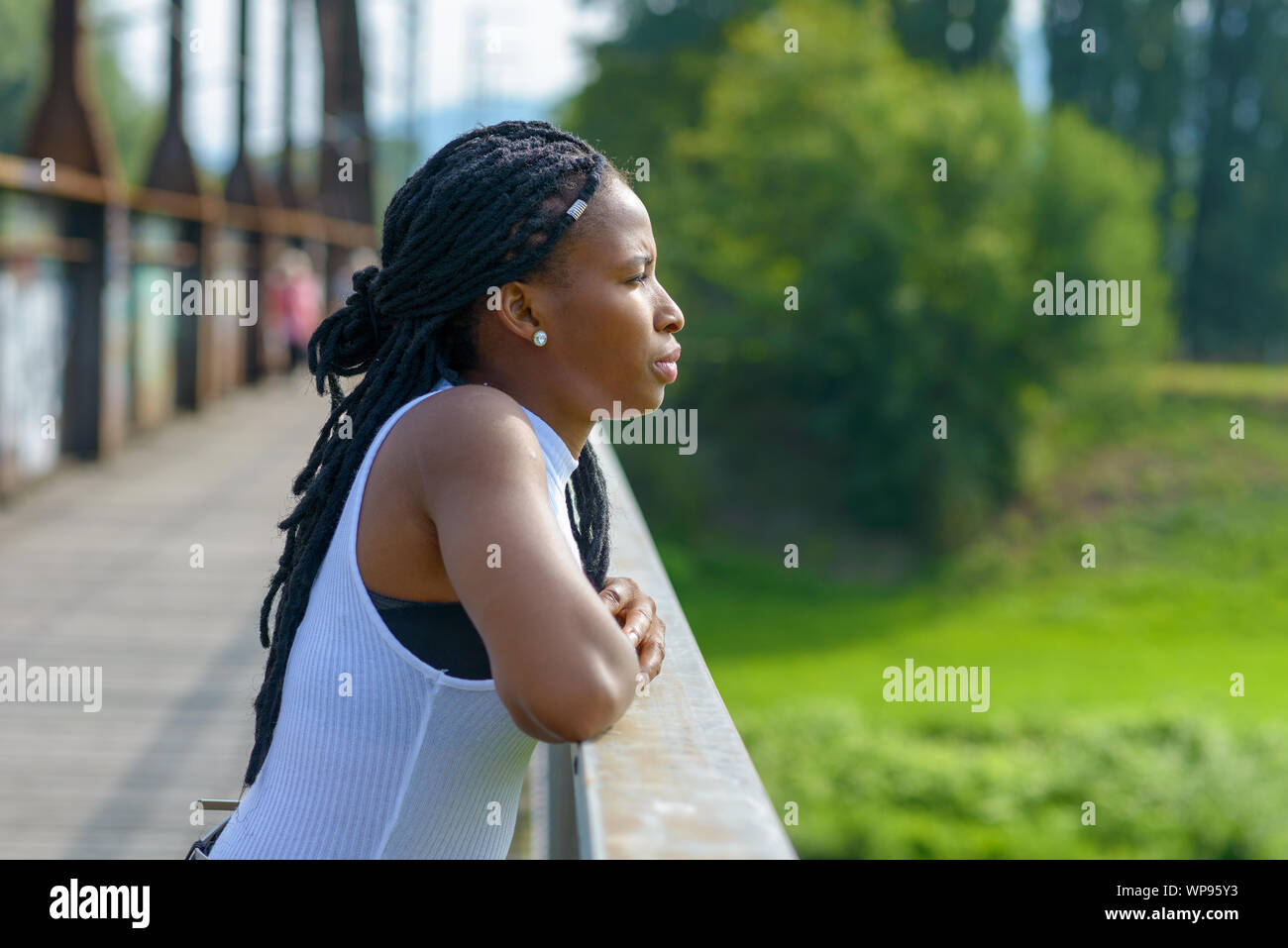 Young African woman standing leaning on the wooden railing staring off ...