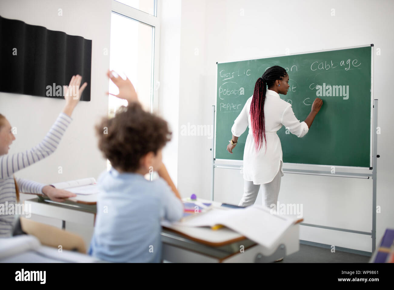 Dark-skinned teacher writing down on blackboard for children Stock ...