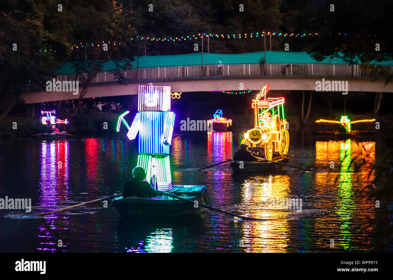 A flotilla of brightly illuminated boats are rowed down the River ...