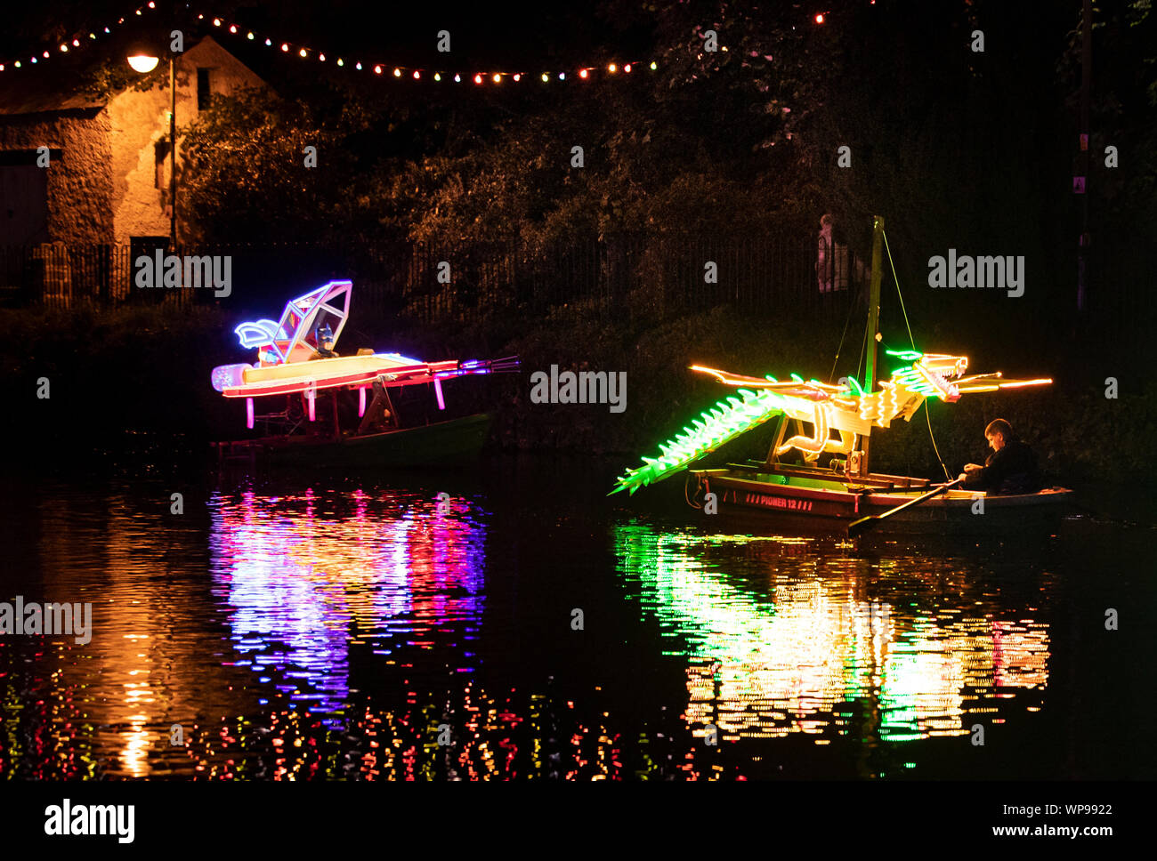A flotilla of brightly illuminated boats are rowed down the River ...