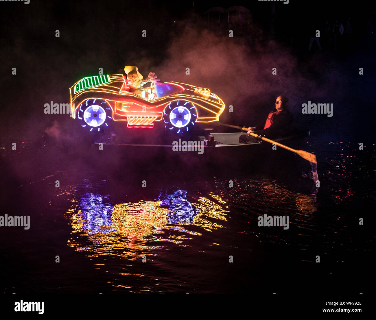 A flotilla of brightly illuminated boats are rowed down the River ...