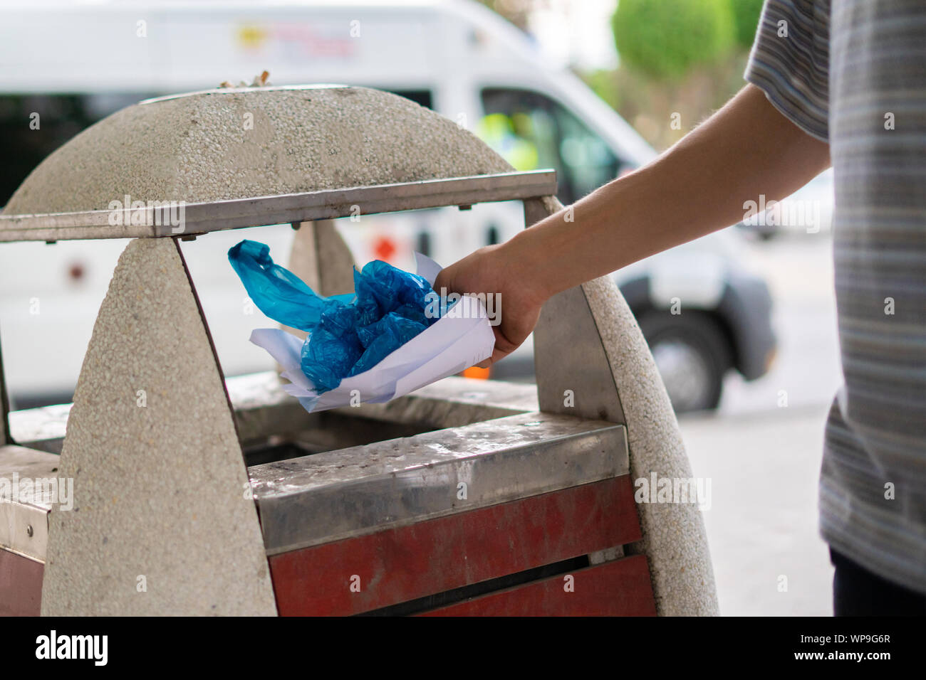 hand throwing paper and plastic garbage into a trash urn in the city ...