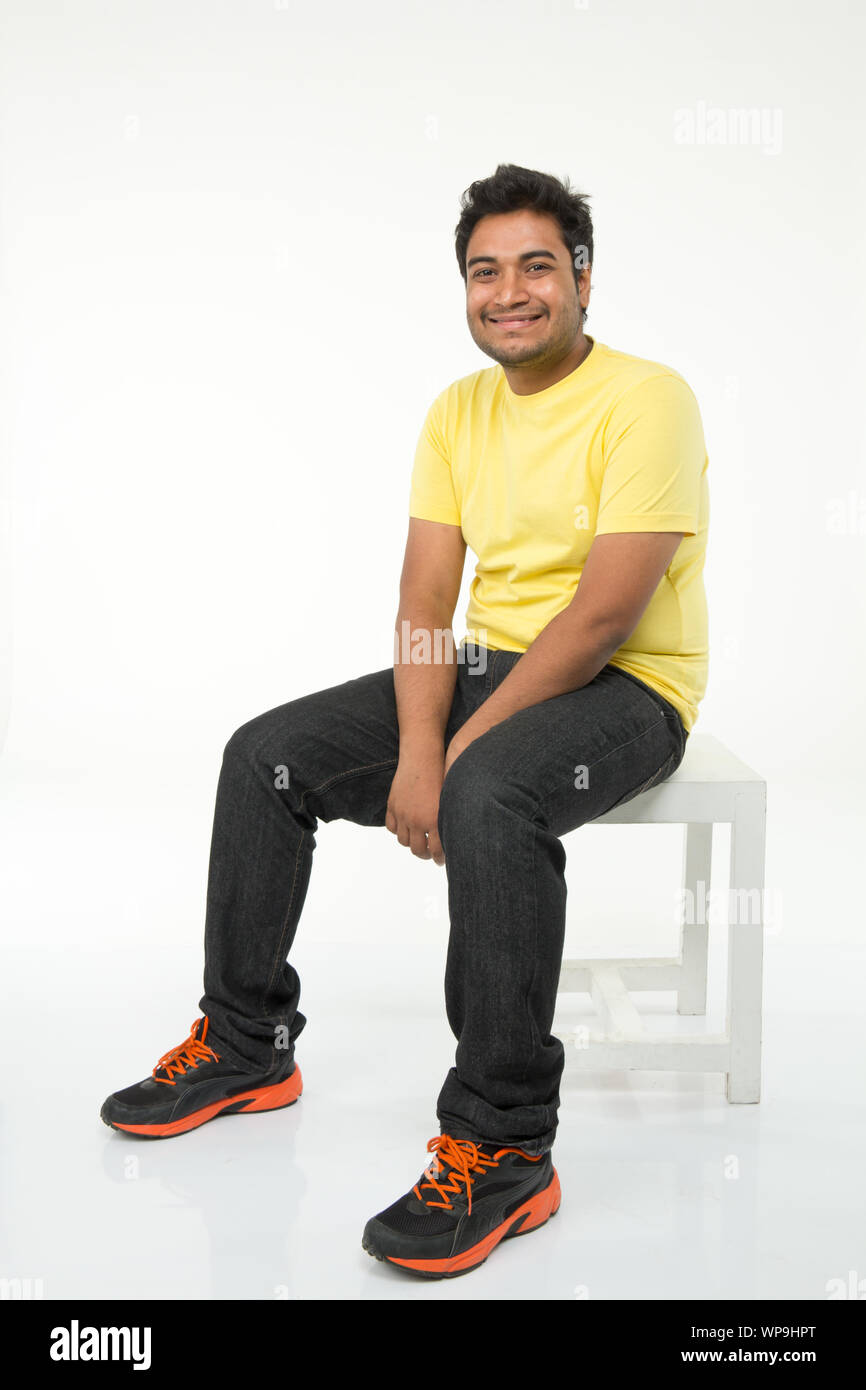 Young man sitting on stool and smiling Stock Photo - Alamy