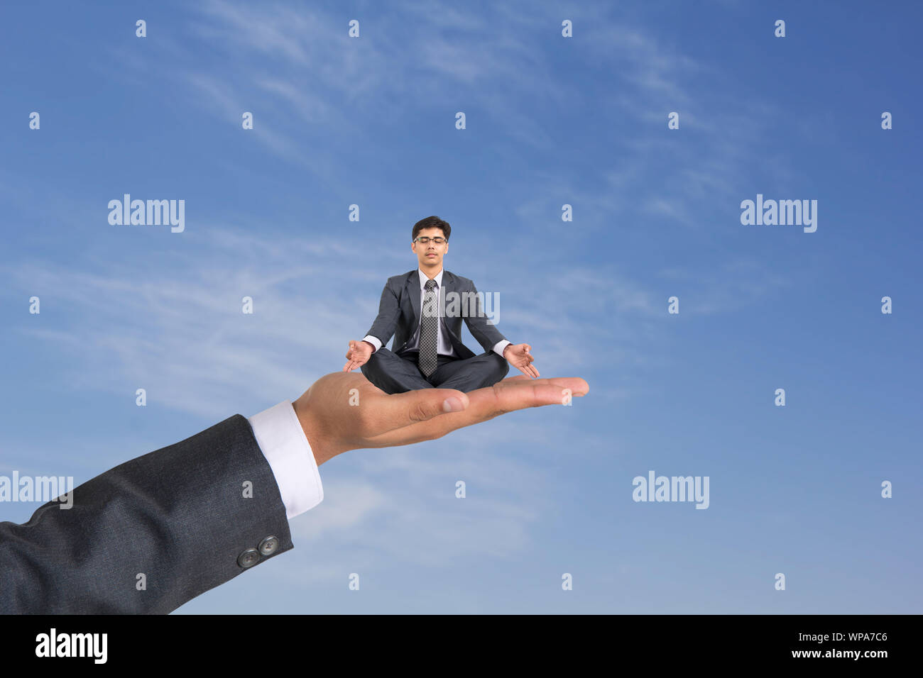 Businessman sitting on human hand and doing yoga pose Stock Photo - Alamy