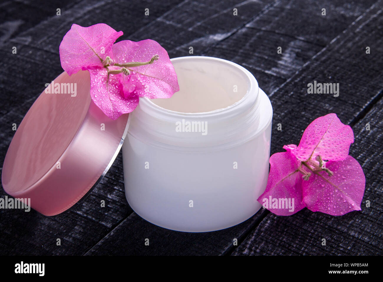 Jar of natural cream with pink flowers on black background. Organic ...