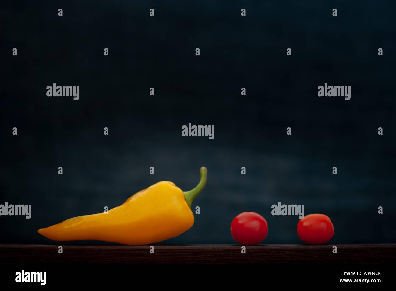 Two red small tomatoes and one large yellow pepper lie in a row on the ...