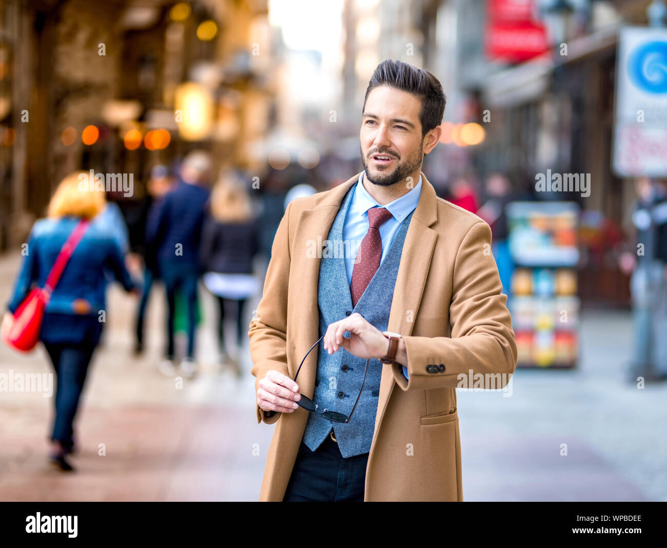 A handsome elegant man walking on the streets and checking the time on ...