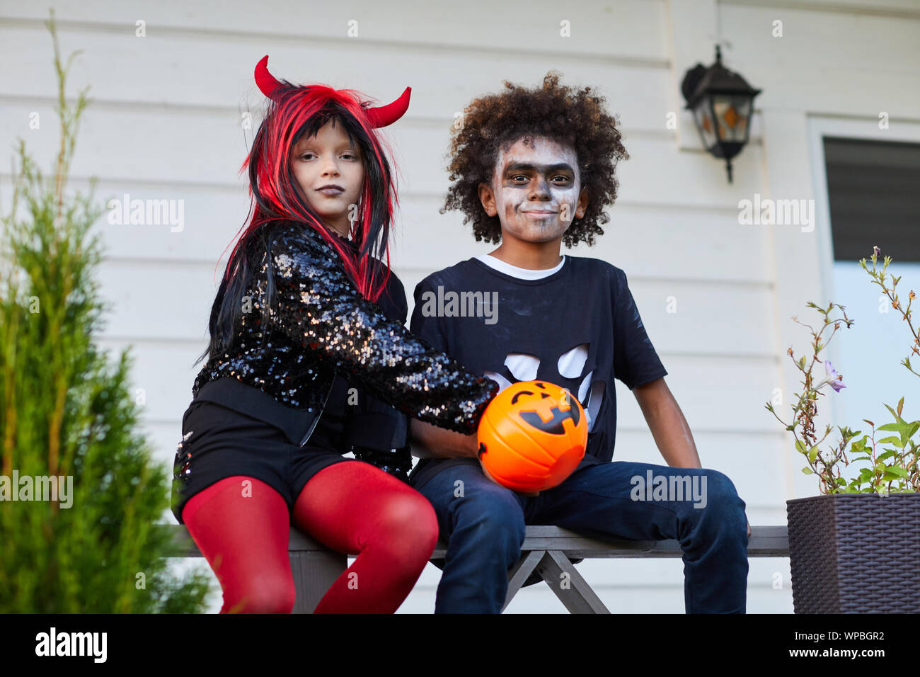 Portrait of two happy kids eating Halloween candy outdoors after trick ...
