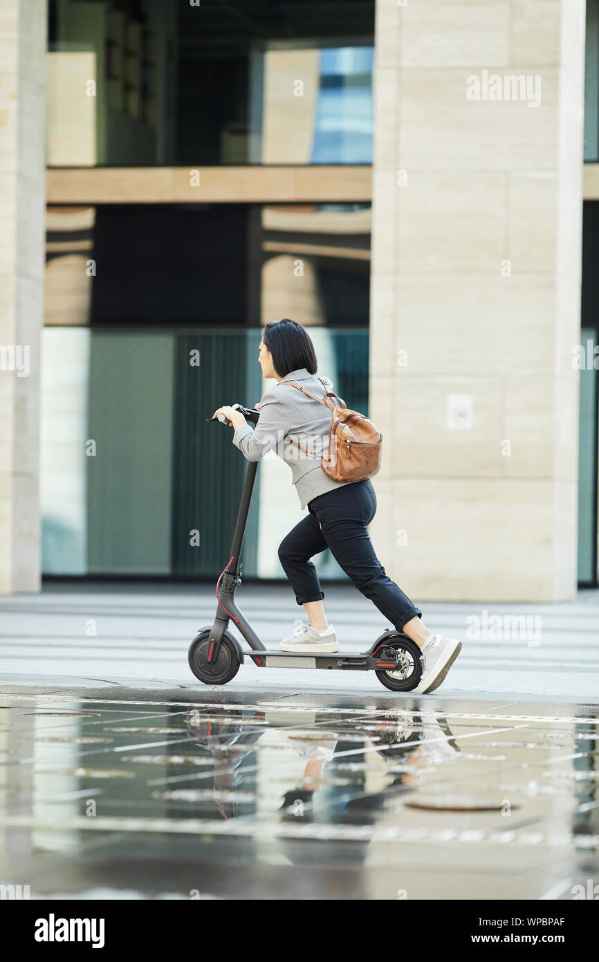 Full length side view of young Asian woman riding electric scooter fast ...
