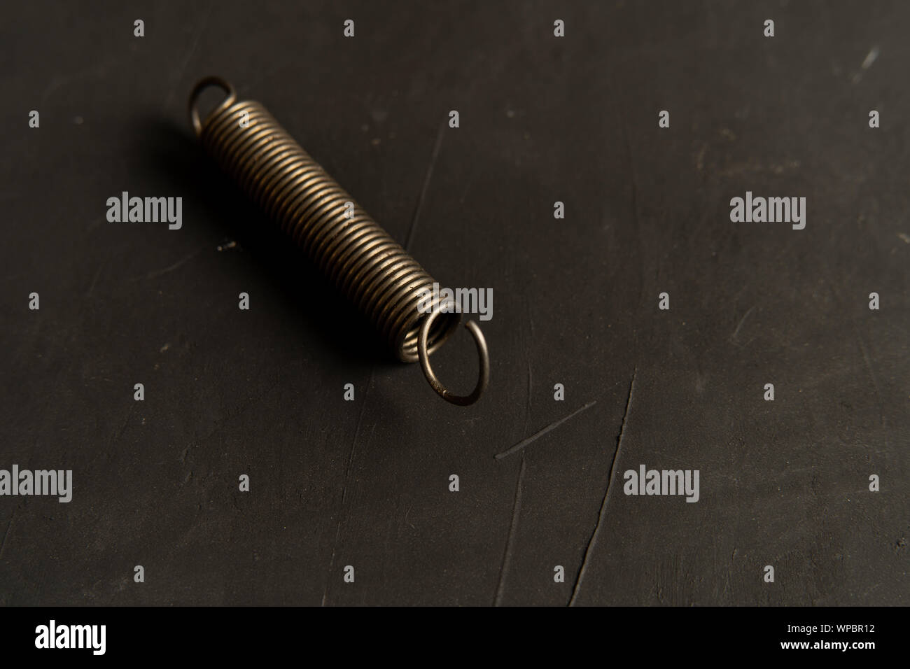 A metal spring with fasteners at the ends lies on a black cement ...