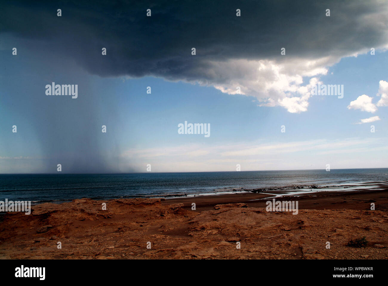 one black cloud, one rain, blue sky and sun light, rocks and ocean in ...