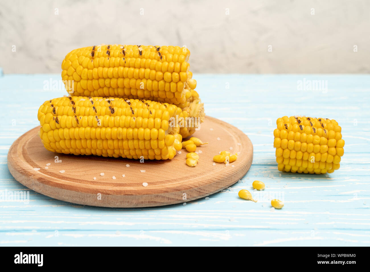 Grilled hot Corn cob lies on round cutting board plate blue wooden ...